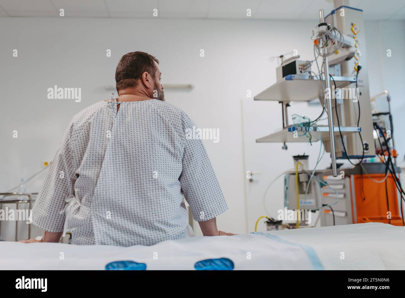 Rear view of overweight patient in hospital gown waiting for medical ...