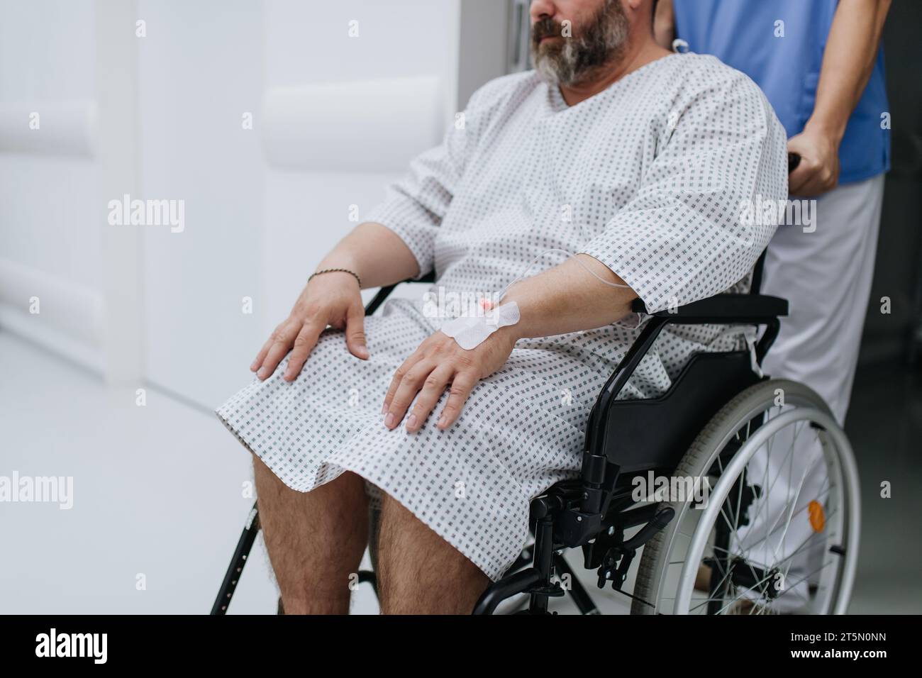 Male nurse pushing a patient in a wheelchair along a hospital corridor ...