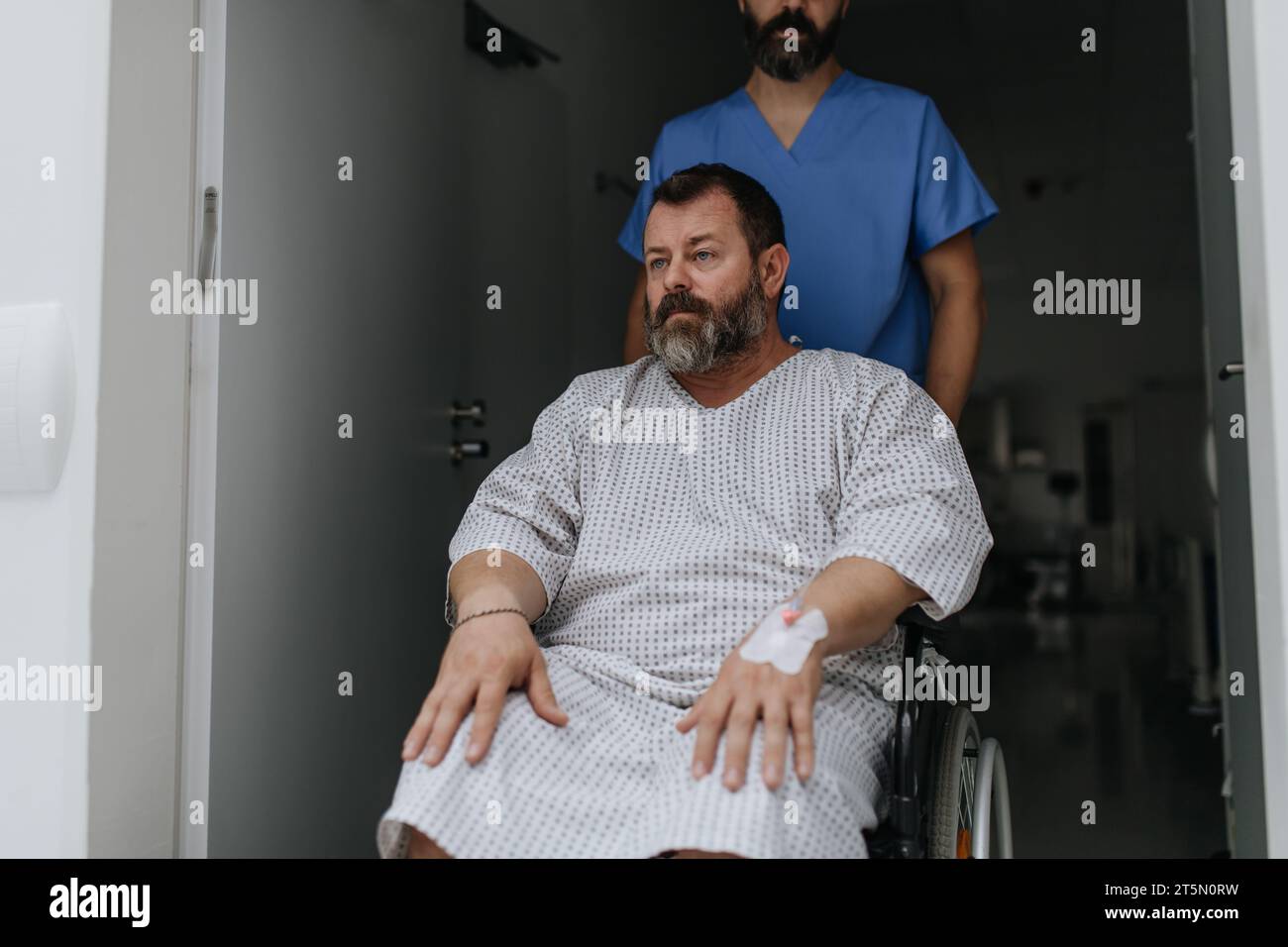 Male nurse pushing a patient in a wheelchair along a hospital corridor ...
