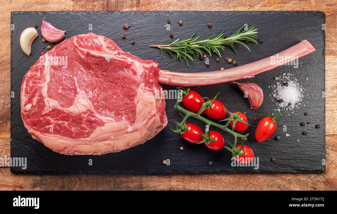 Raw rib steak with bone or tomahawk steak with seasonings on slate ...