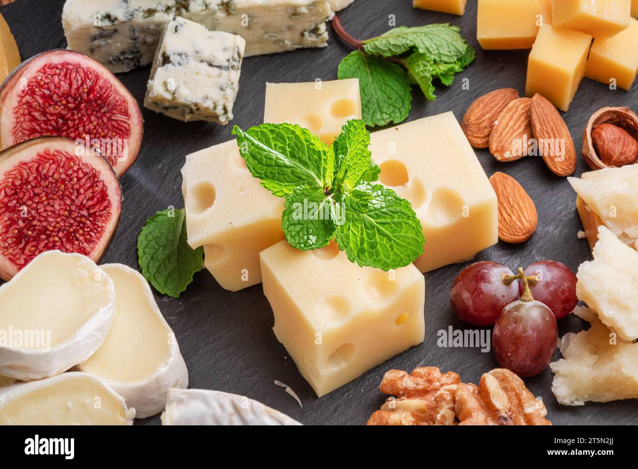 Variety of sliced cheeses with fruits, mint, nuts and cheese cutting ...