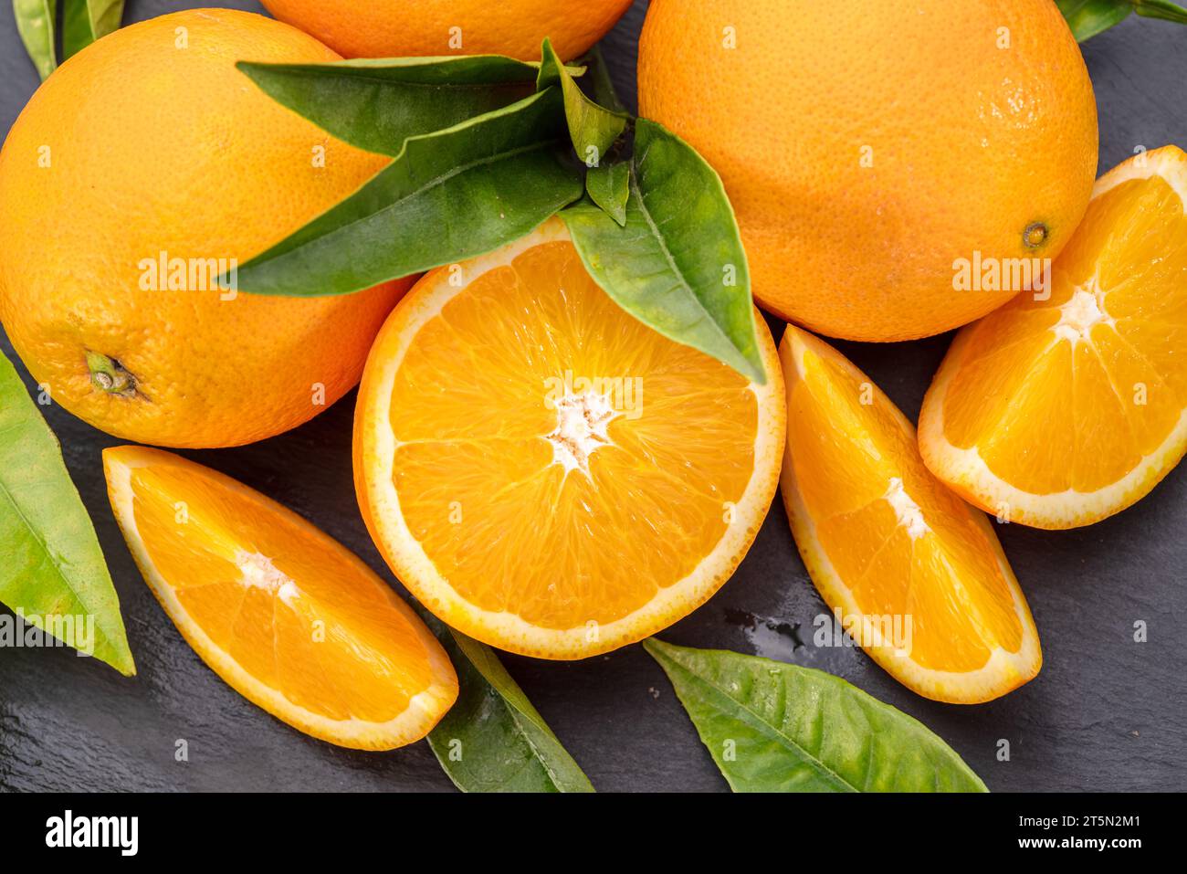 Ripe orange fruits with slices and orange tree leaves on a gray stone ...