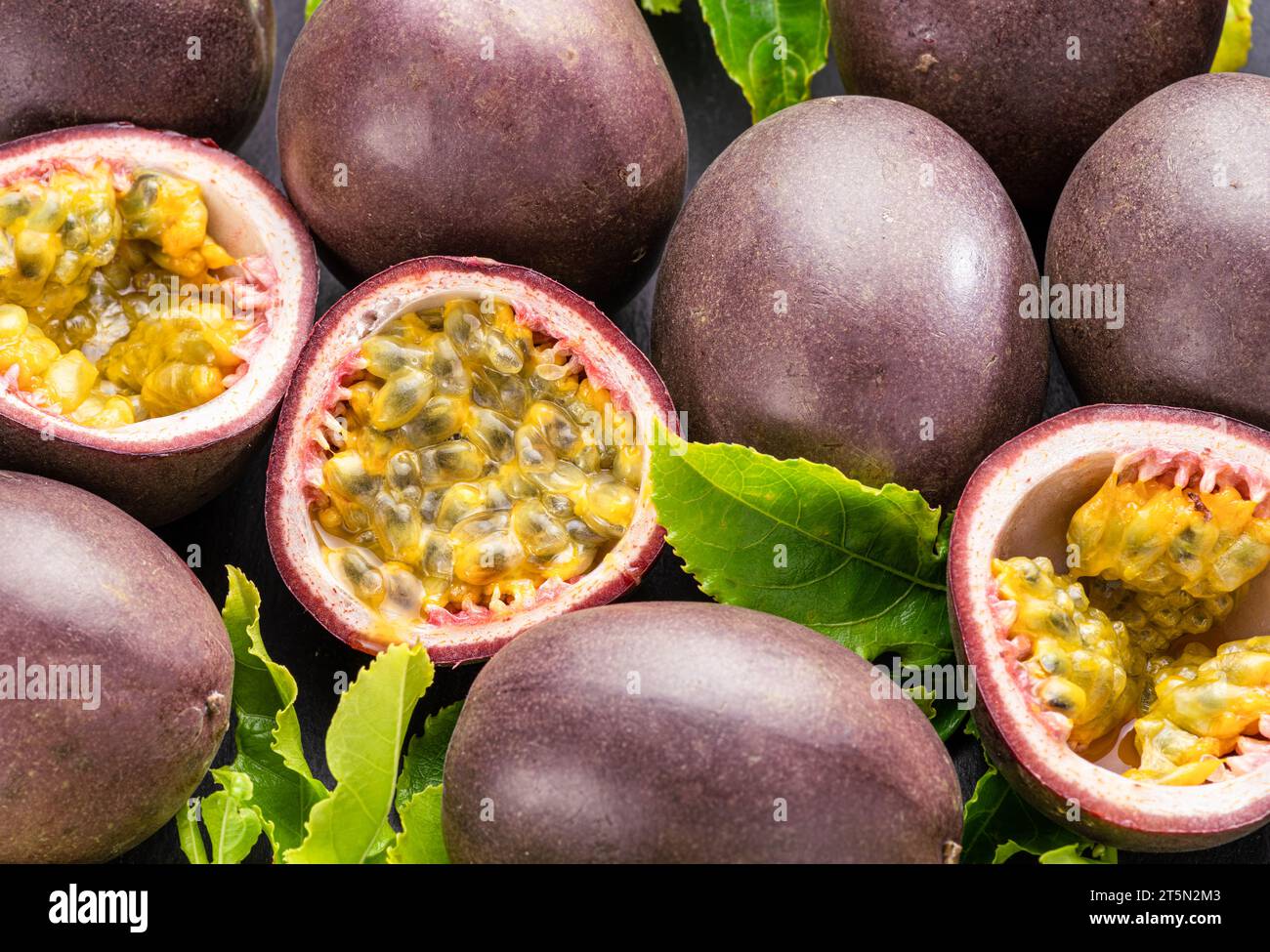 Ripe passion fruits with passion fruit seeds and passionfruit leaves on a gray stone table. Nice ...