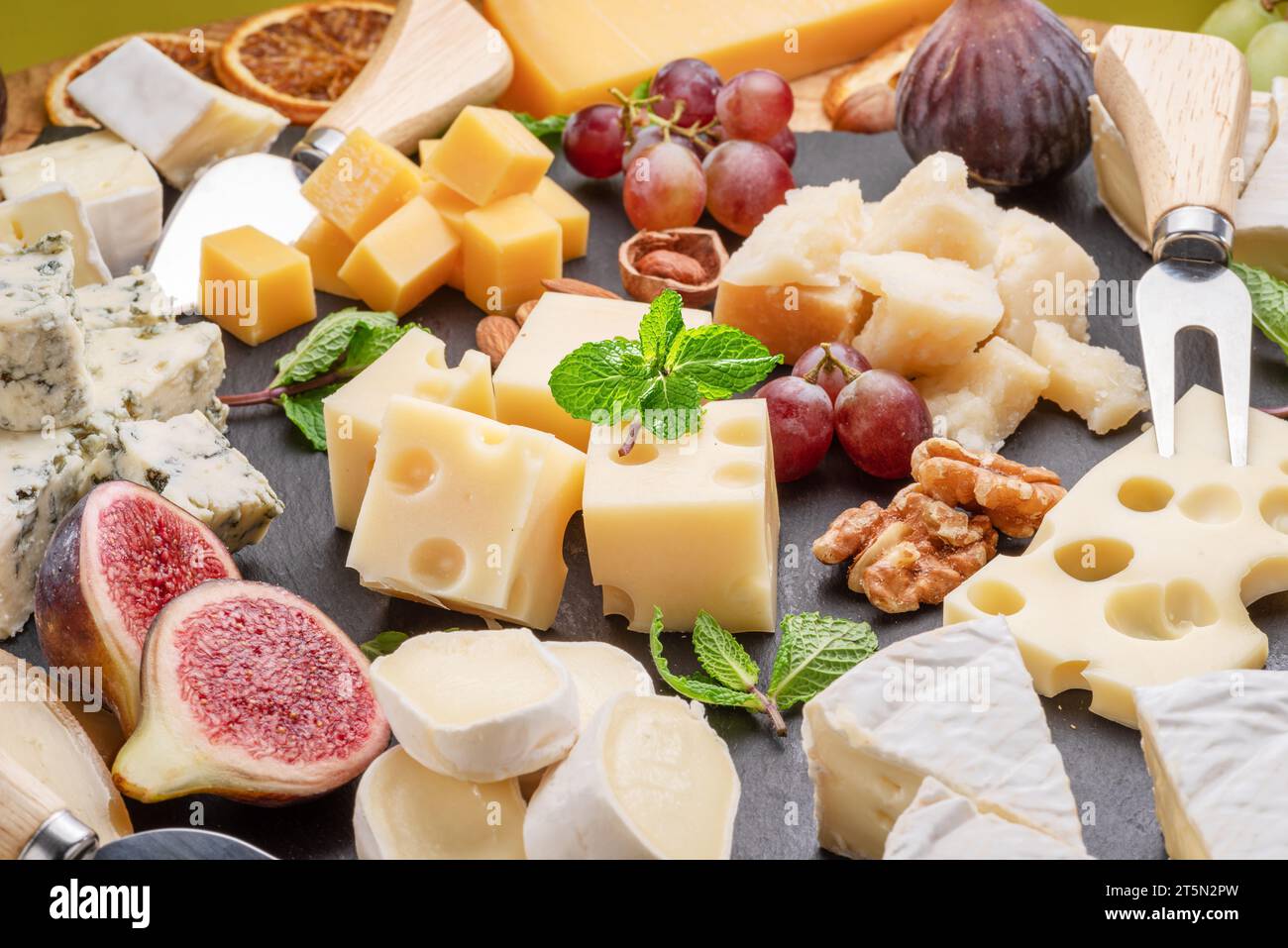 Variety of sliced cheeses with fruits, mint, nuts and cheese cutting ...