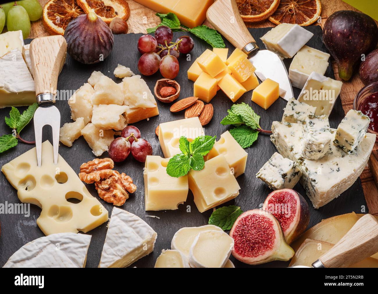 Variety of sliced cheeses with fruits, mint, nuts and cheese cutting ...