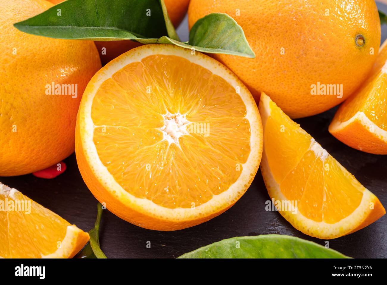 Ripe orange fruits with slices and orange tree leaves on a gray stone ...