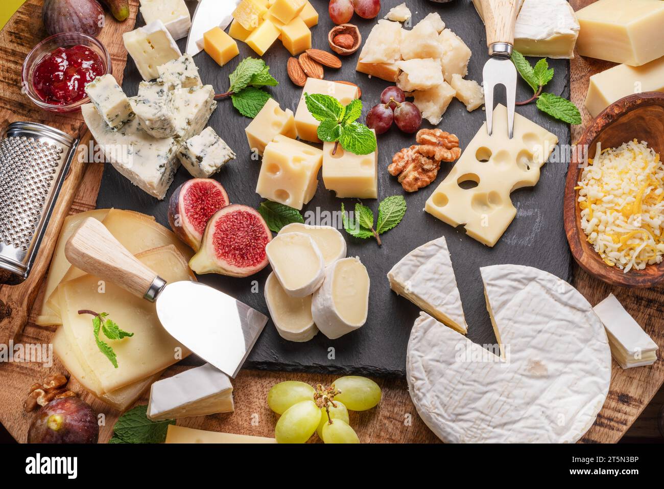 Variety of sliced cheeses with fruits, mint, nuts and cheese cutting ...