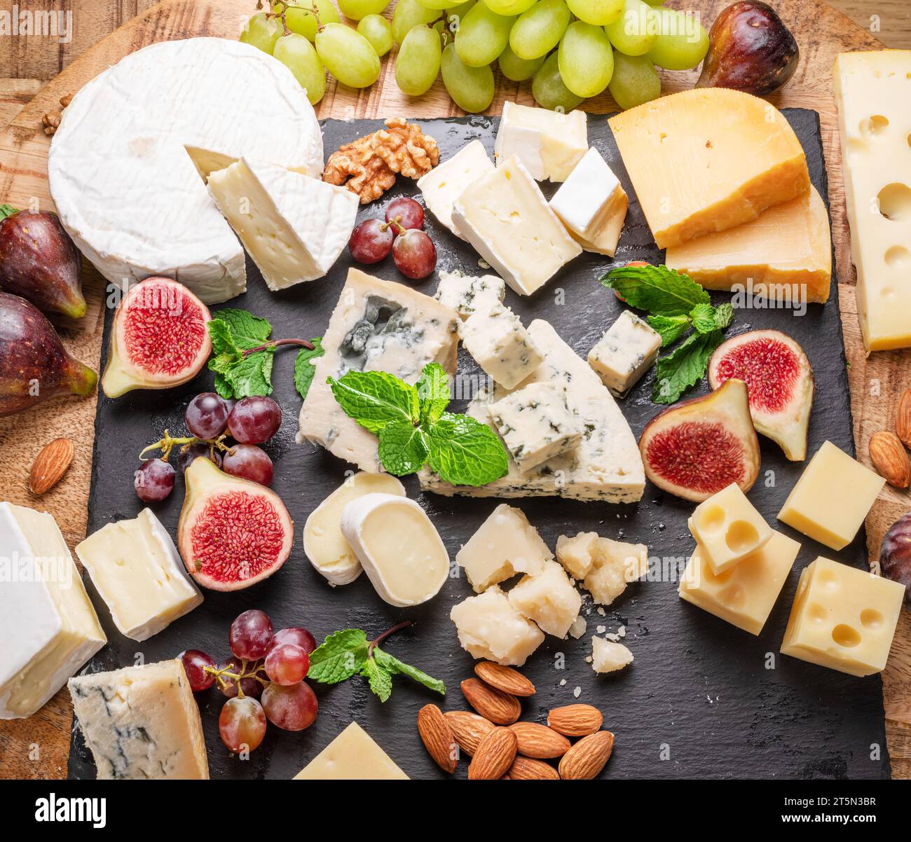 Variety of sliced cheeses with fruits, mint, nuts and cheese cutting ...