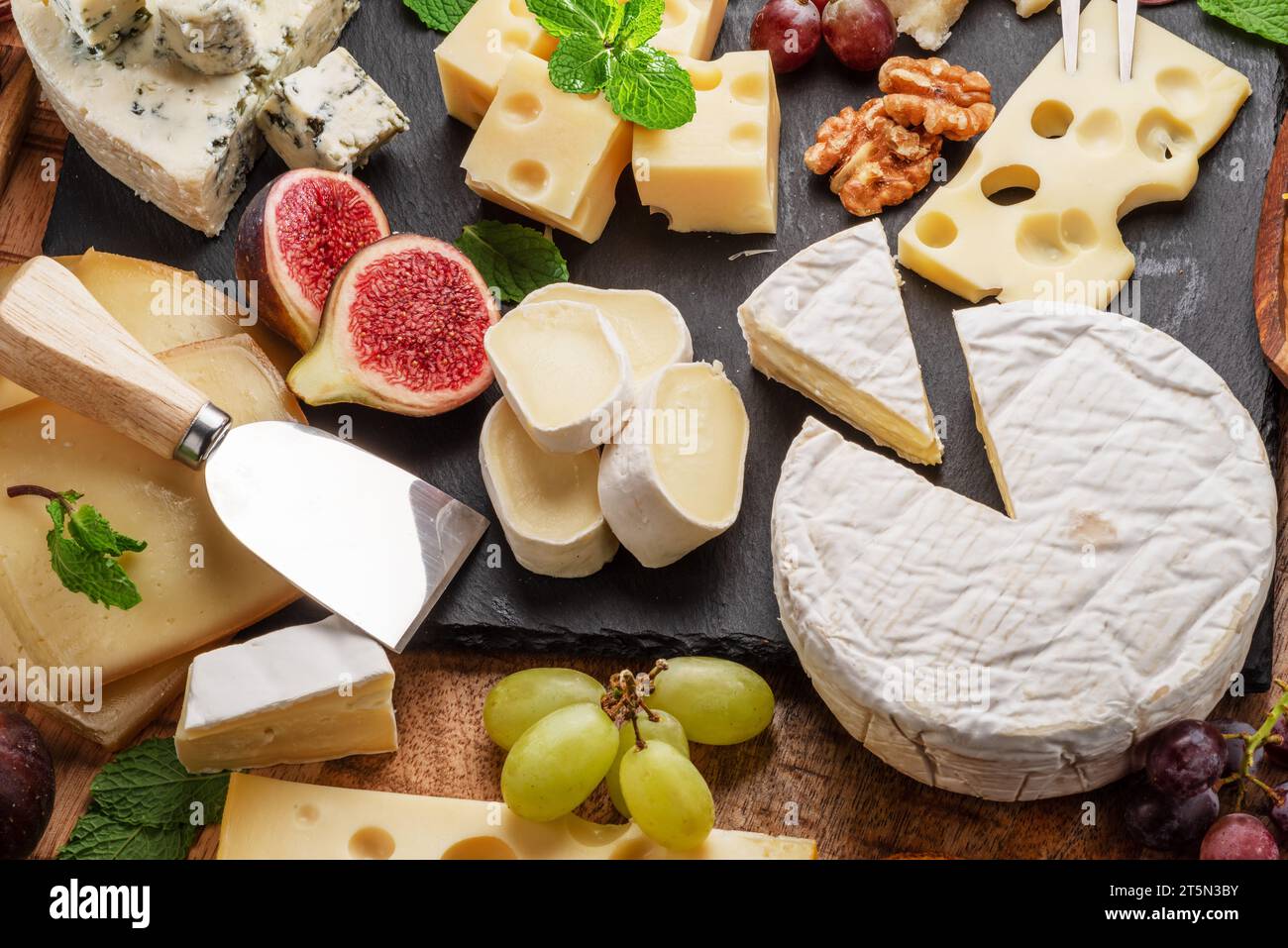 Variety of sliced cheeses with fruits, mint, nuts and cheese cutting ...