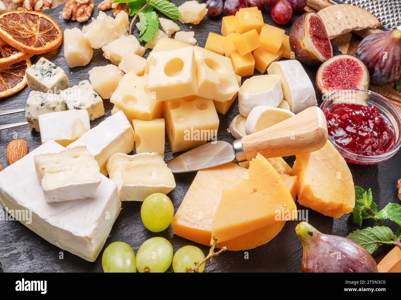 Variety of sliced cheeses with fruits, mint, nuts and cheese cutting ...
