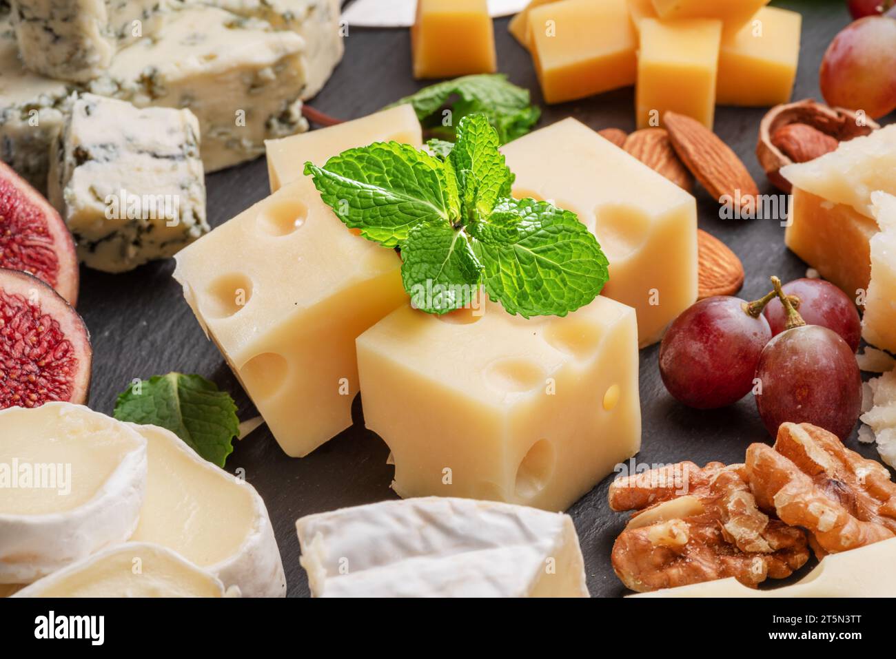 Variety of sliced cheeses with fruits, mint, nuts and cheese cutting ...