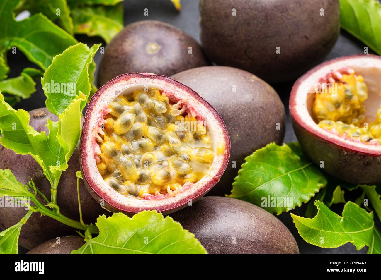 Ripe passion fruits with passion fruit seeds and passionfruit leaves on a gray stone table. Nice ...