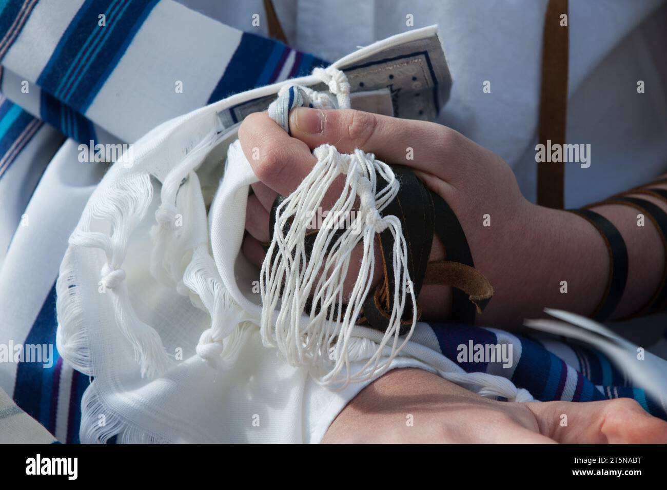A Jewish man grasps the strings of his tallit or tzitzit while reciting ...