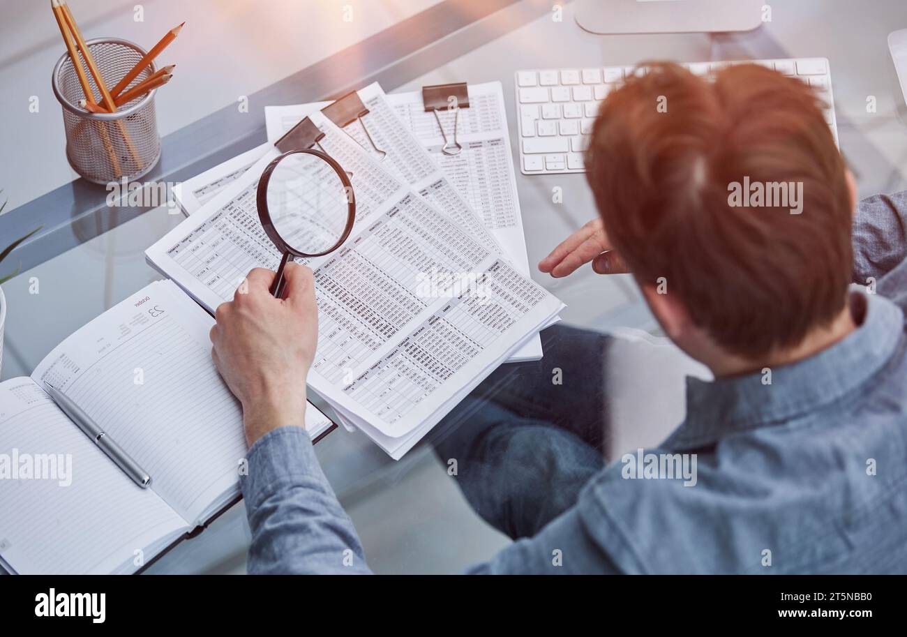 Businessman looking through a magnifying glass to documents note in the ...