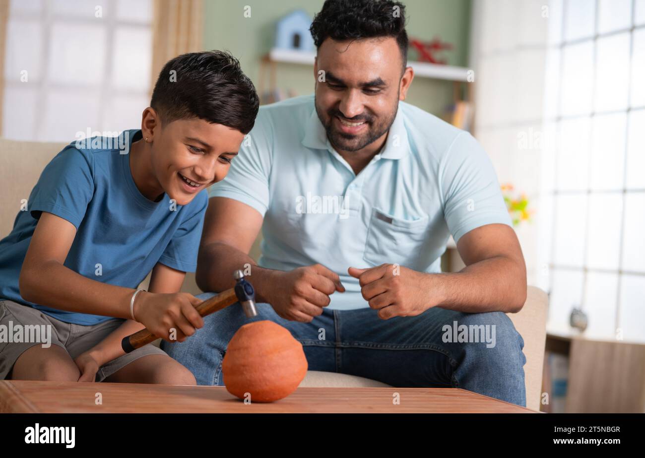 Excited indian father with son breaking clay money pot or piggy bank by ...