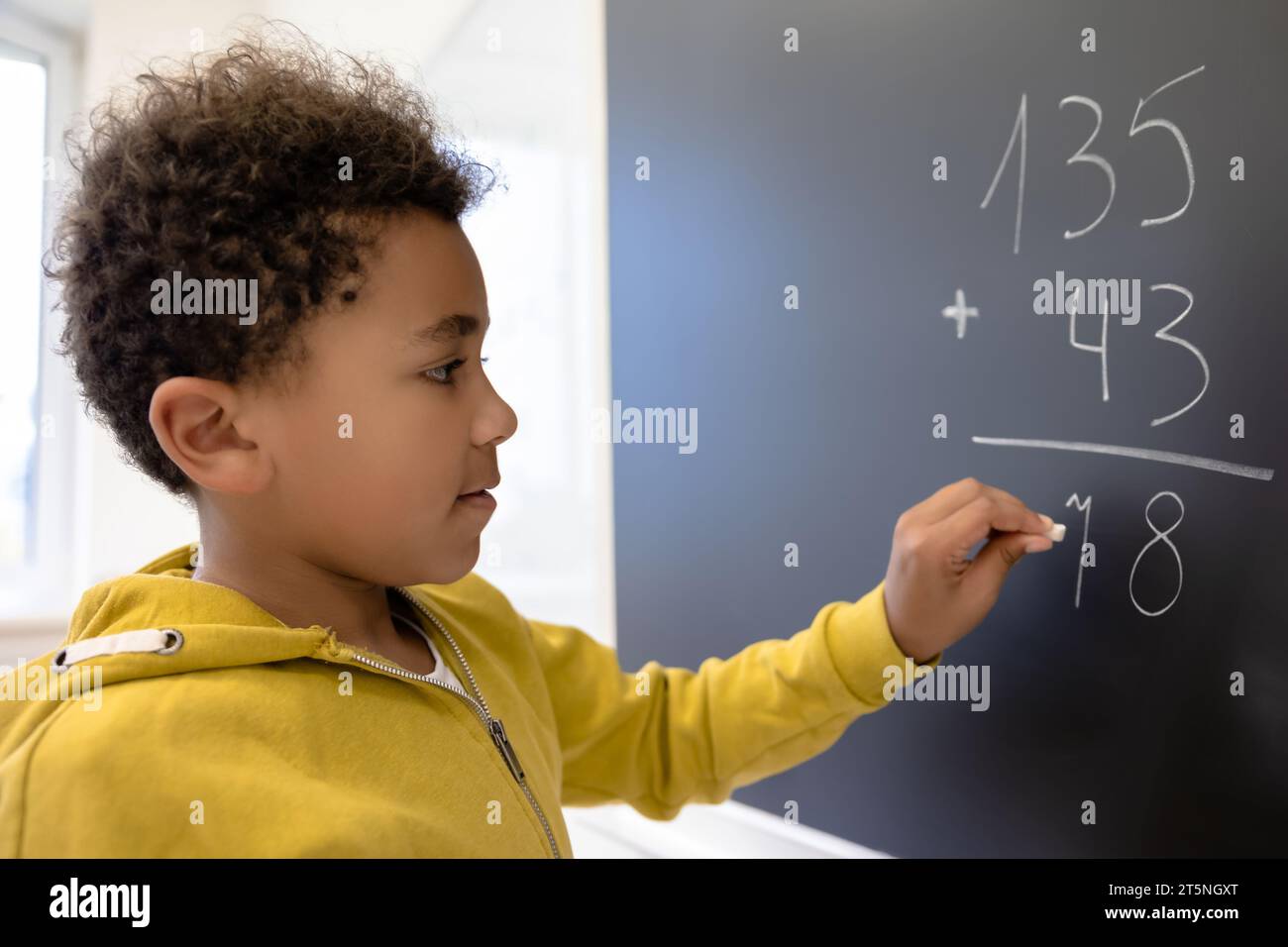 The dark-skinned boy writing fraction on the board at maths lesson ...