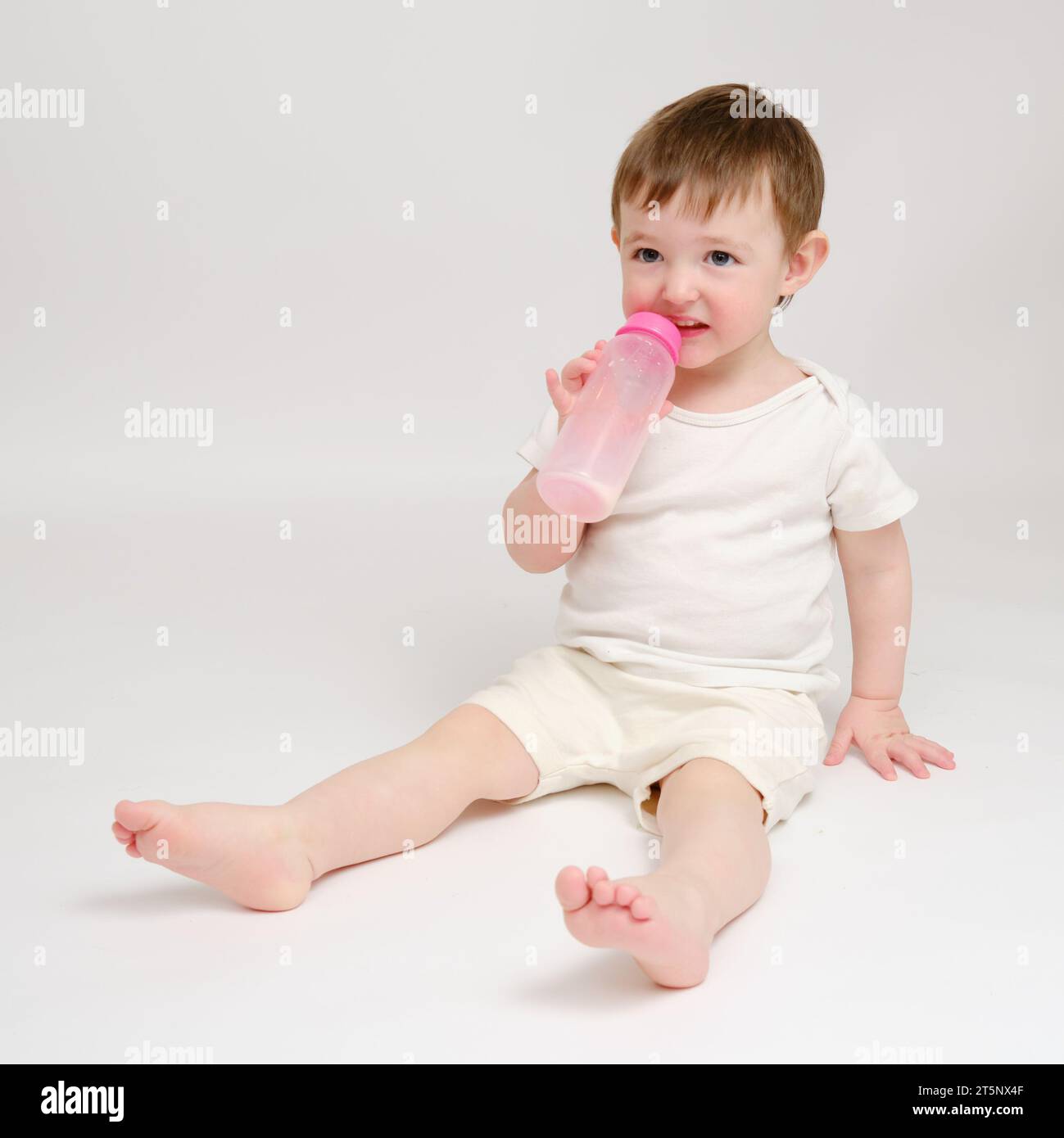 Happy baby drinks milk from bottle on studio white background. Resting ...