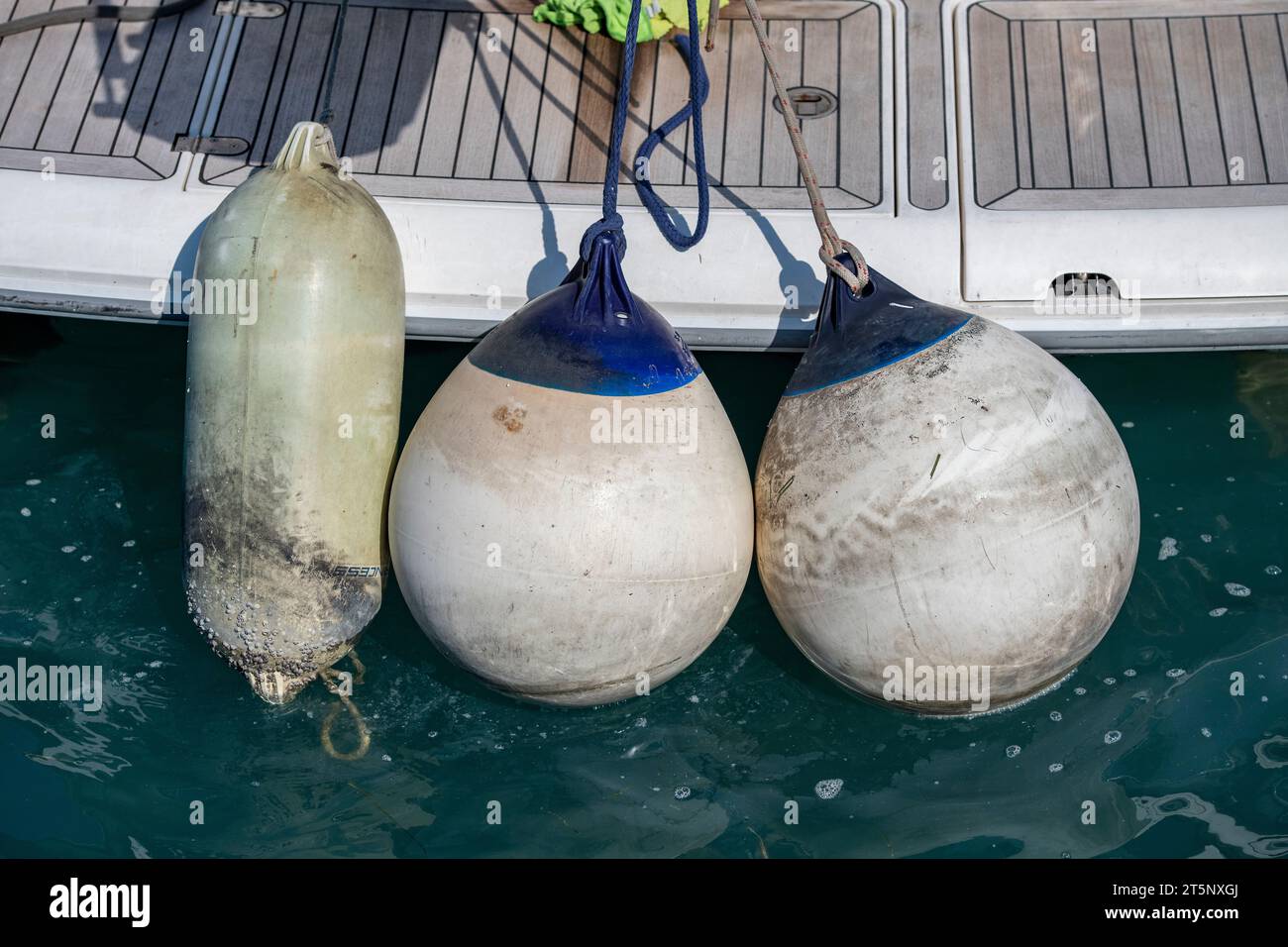 three dirty old pneumatic boat fenders hanging on the stern of a large ...