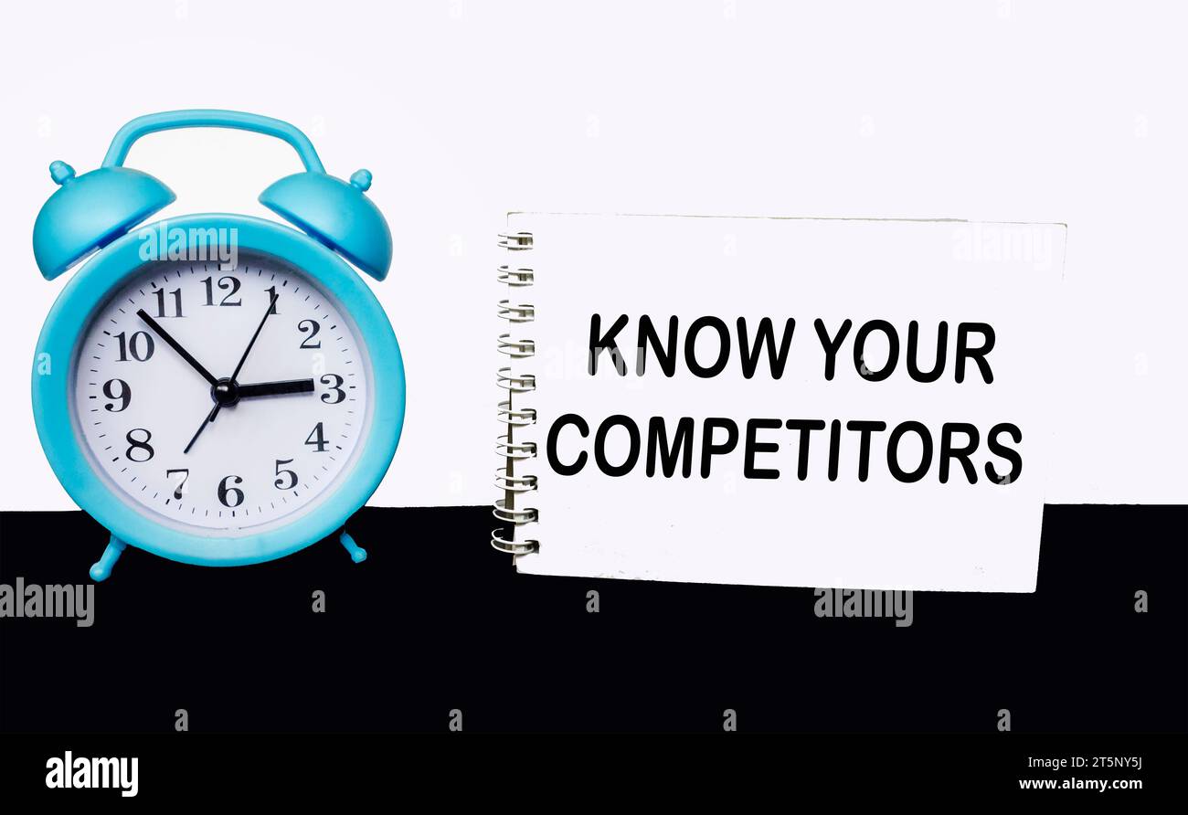 View of a notepad with the text KNOW YOUR COMPETITORS, clock on a black ...