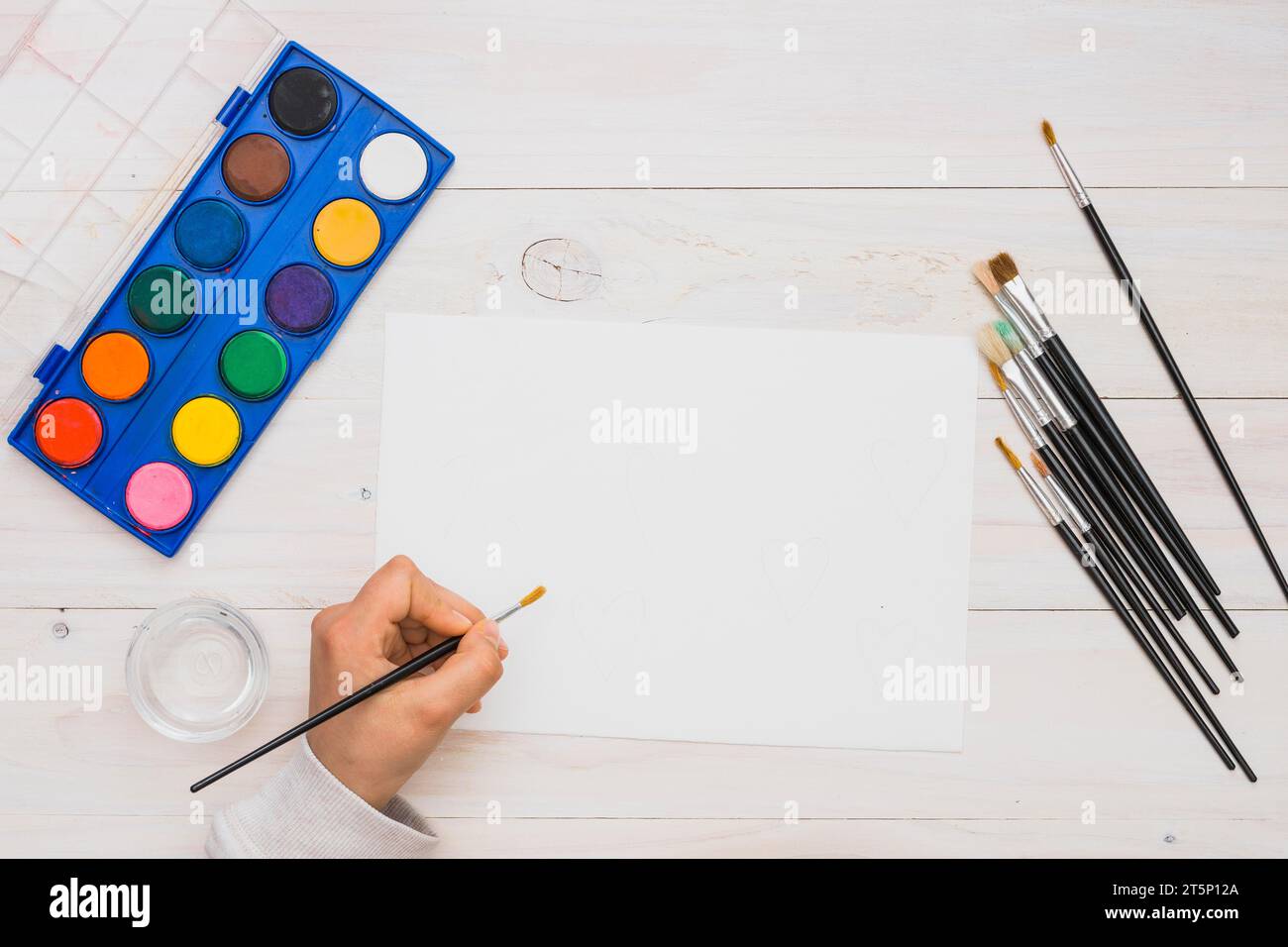 Overhead view human hand painting white blank paper with paint brush ...
