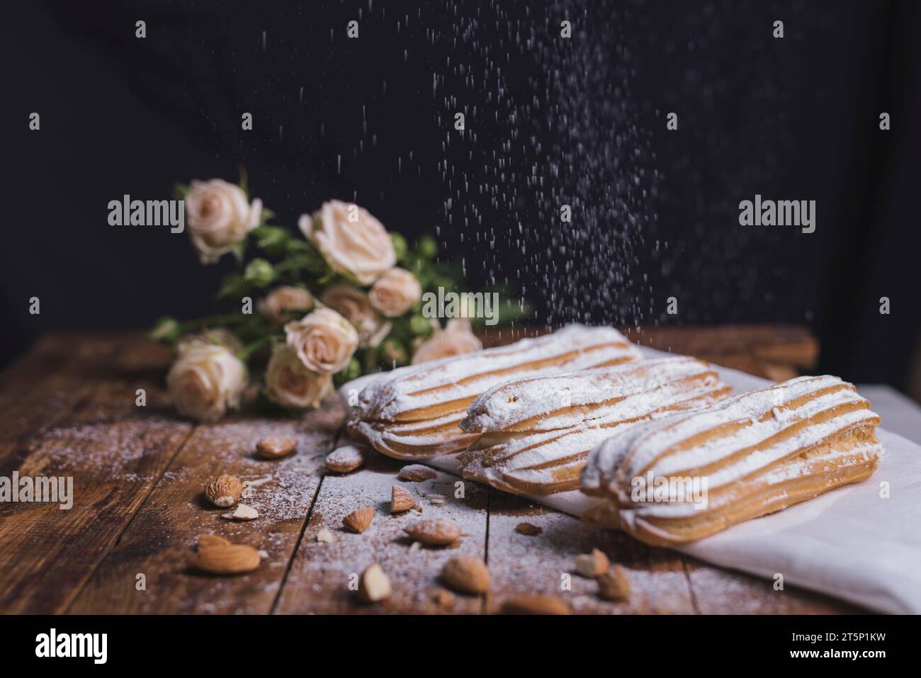 Sugar powder dusted baked eclairs with almonds wooden backdrop Stock ...