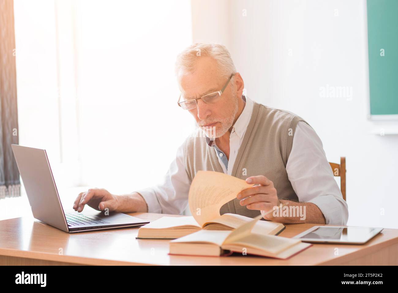 Aged professor male working with laptop while reading book classroom ...