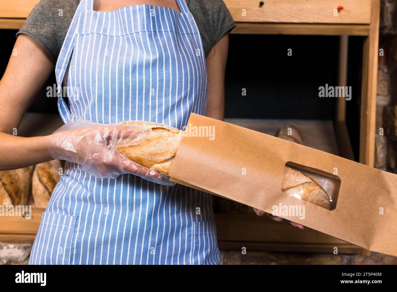 Female baker apron packing baguette bread brown paper bag Stock Photo ...