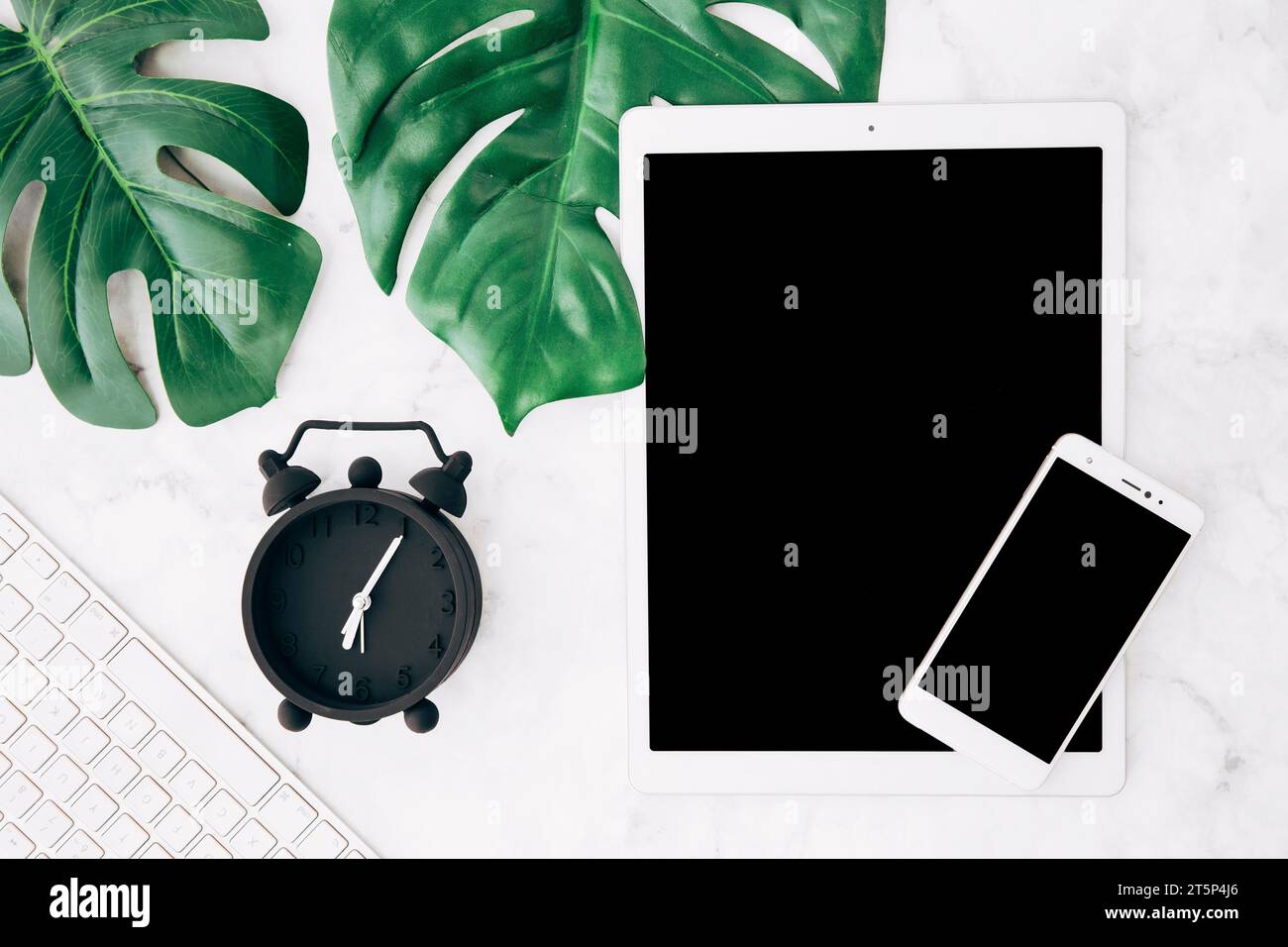 Green monstera leaves alarm clock keyboard digital tablet mobile phone ...