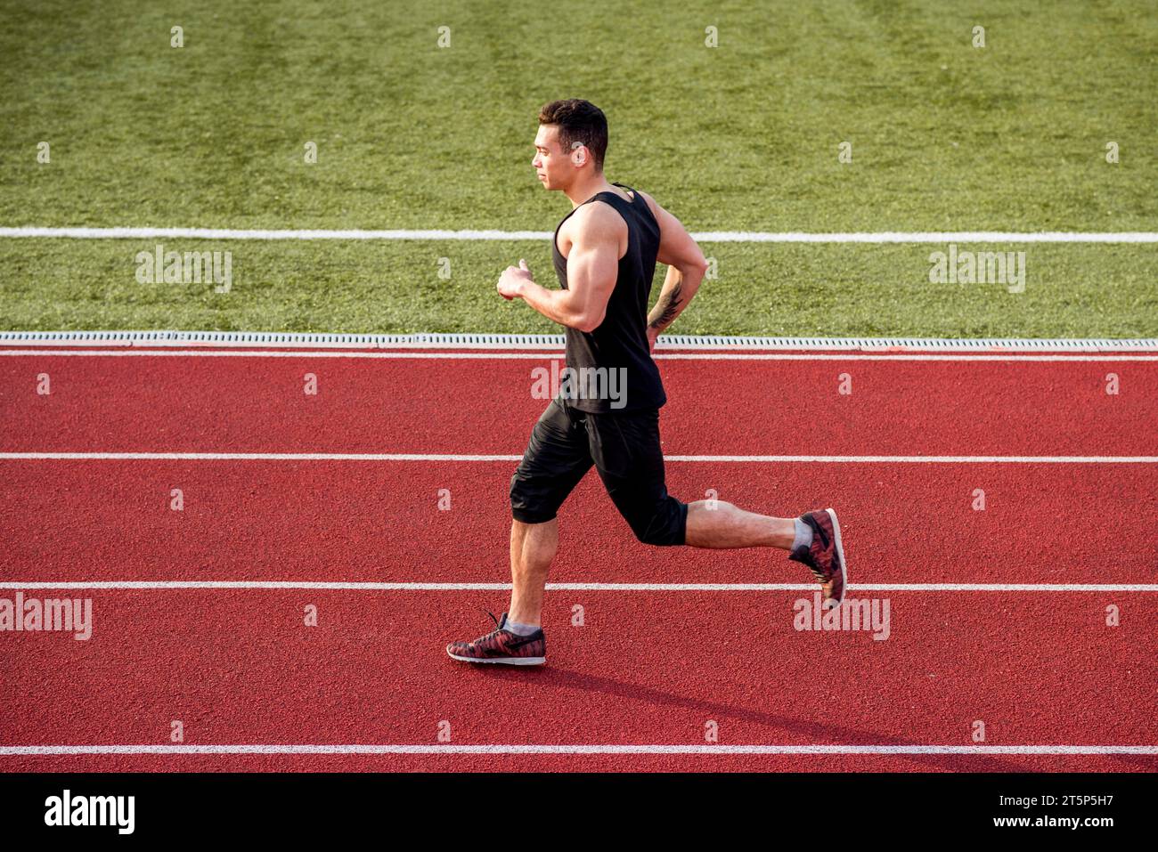 Muscular male runner running red race track Stock Photo - Alamy