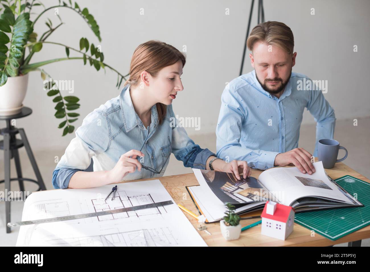 Professional male female architect looking catalog while working office ...