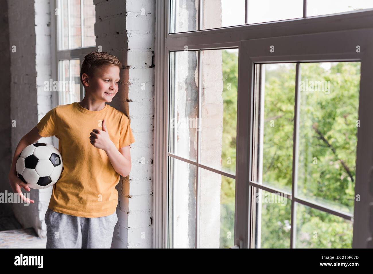 Smiling boy holding soccer ball looking out through window Stock Photo ...