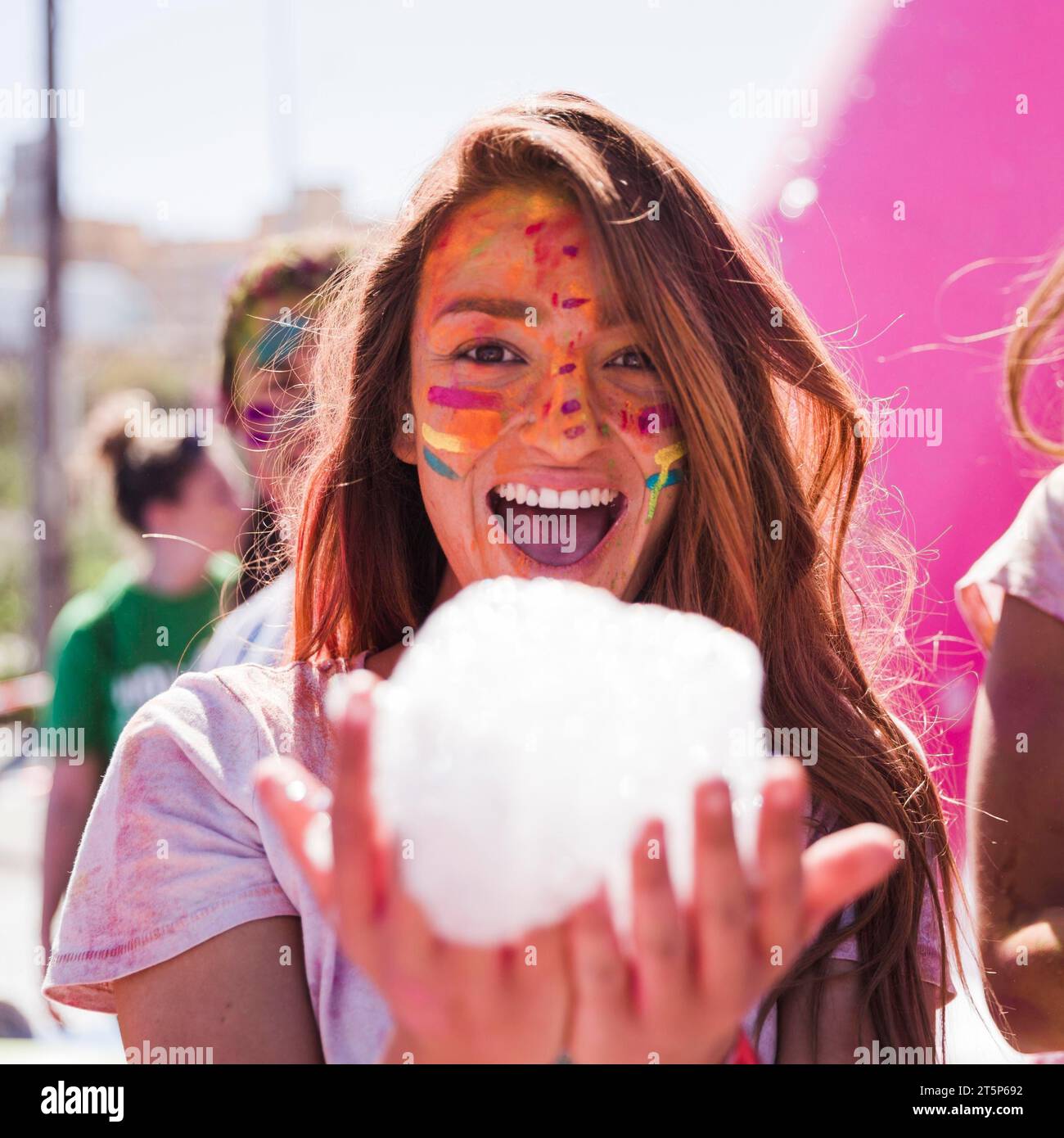 Smiling young woman with holi color her face holding foam hand looking ...