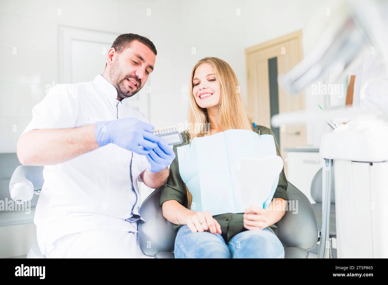 Dentist assisting happy female patient while choosing color tone her teeth Stock Photo - Alamy