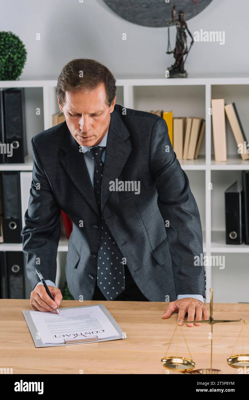 Mature male lawyer signing contract document front justice scale Stock ...