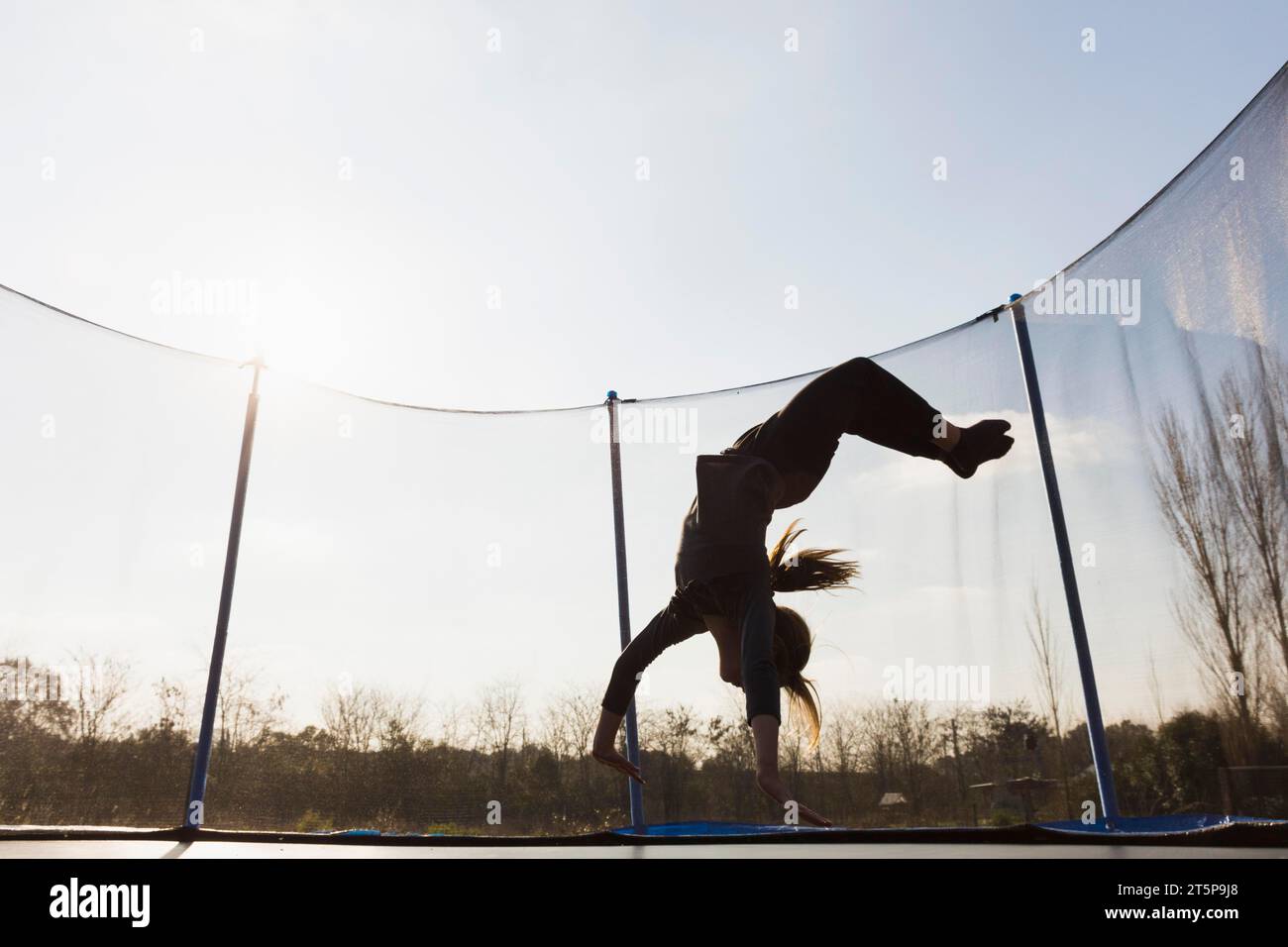 Silhouette girl jumping upside down trampoline against blue sky Stock ...