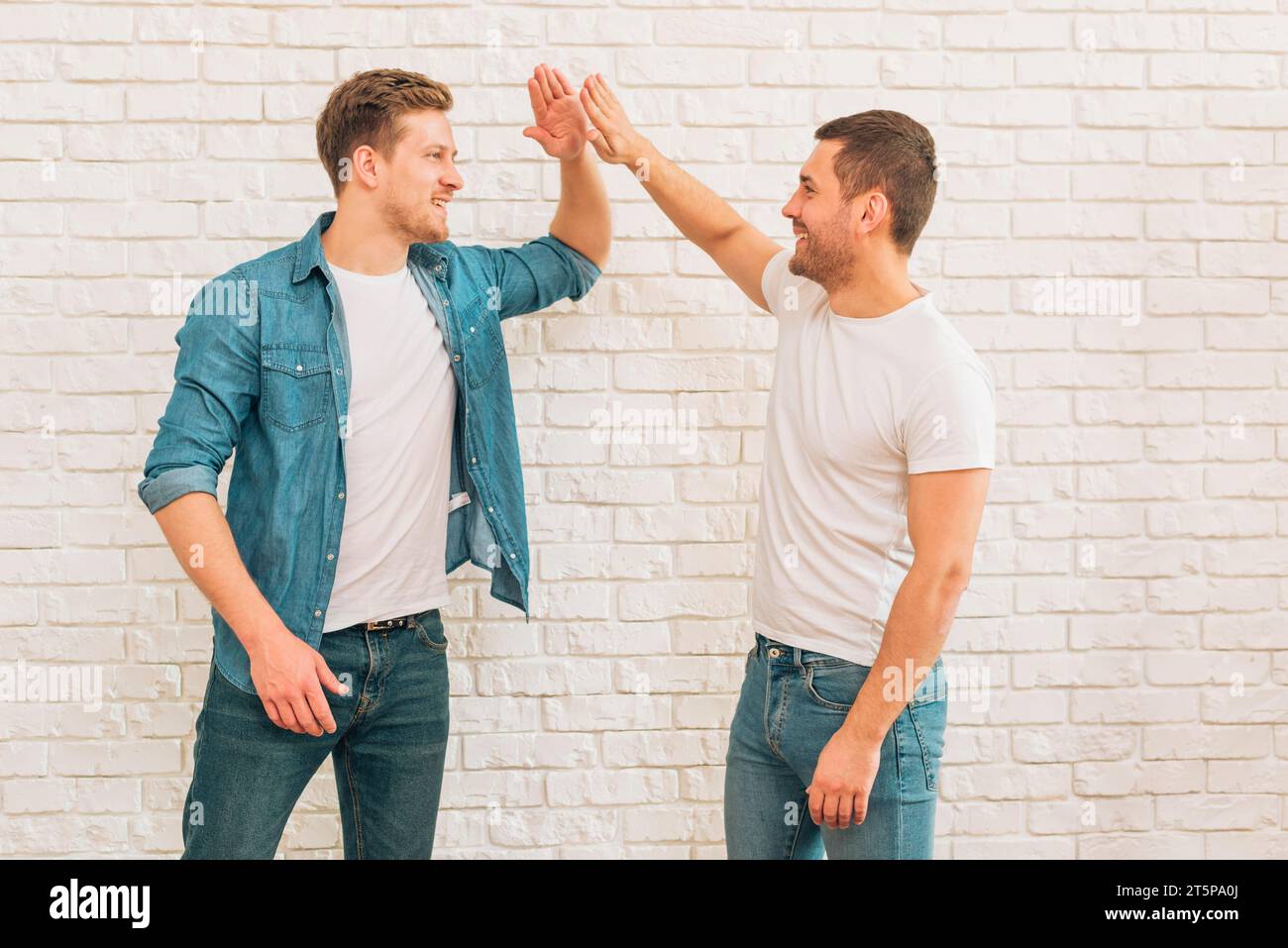 Two male friends giving high five each other against white brick wall ...