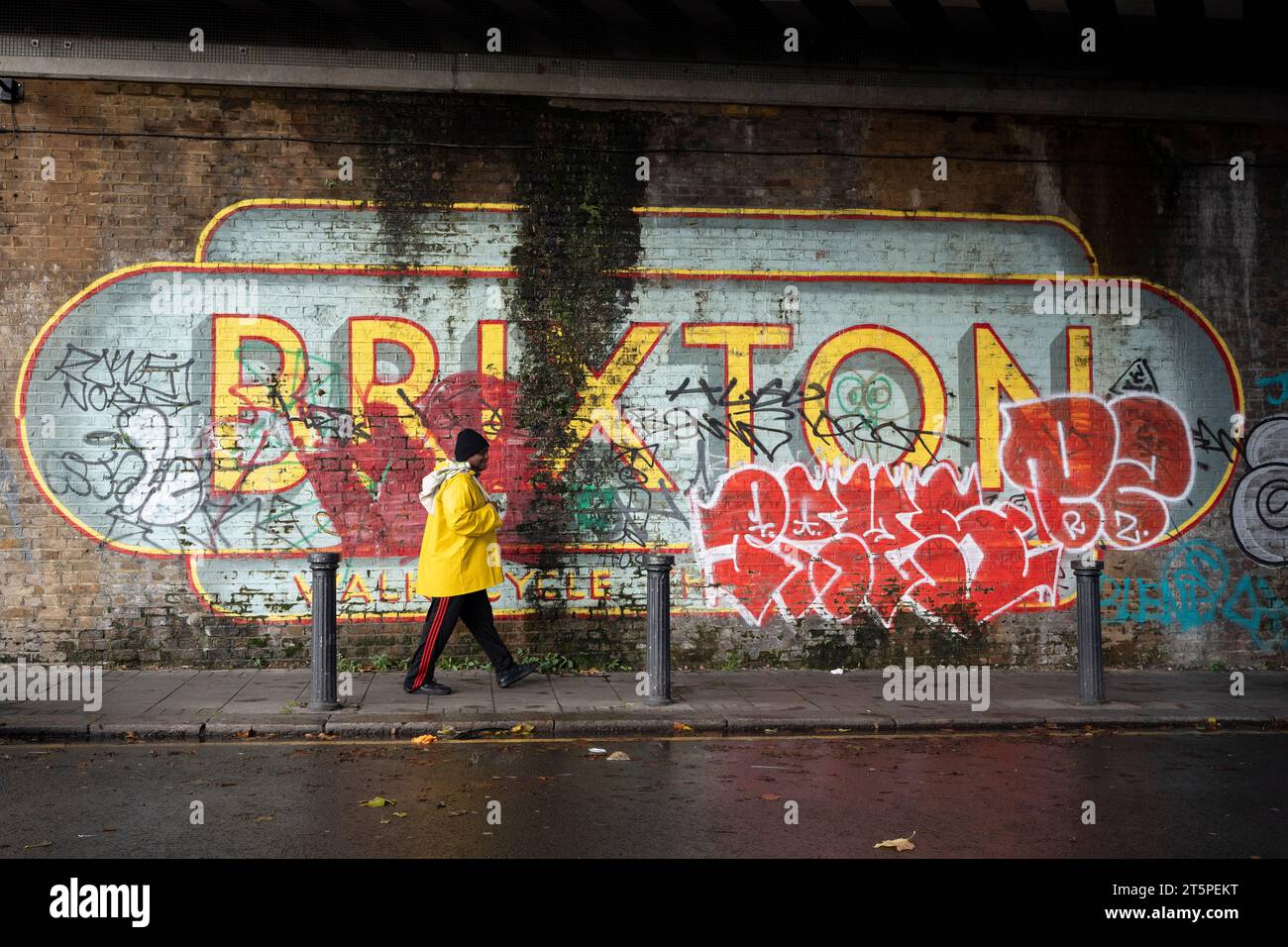 South Londoners walk under a railway bridge and past a large mural of ...