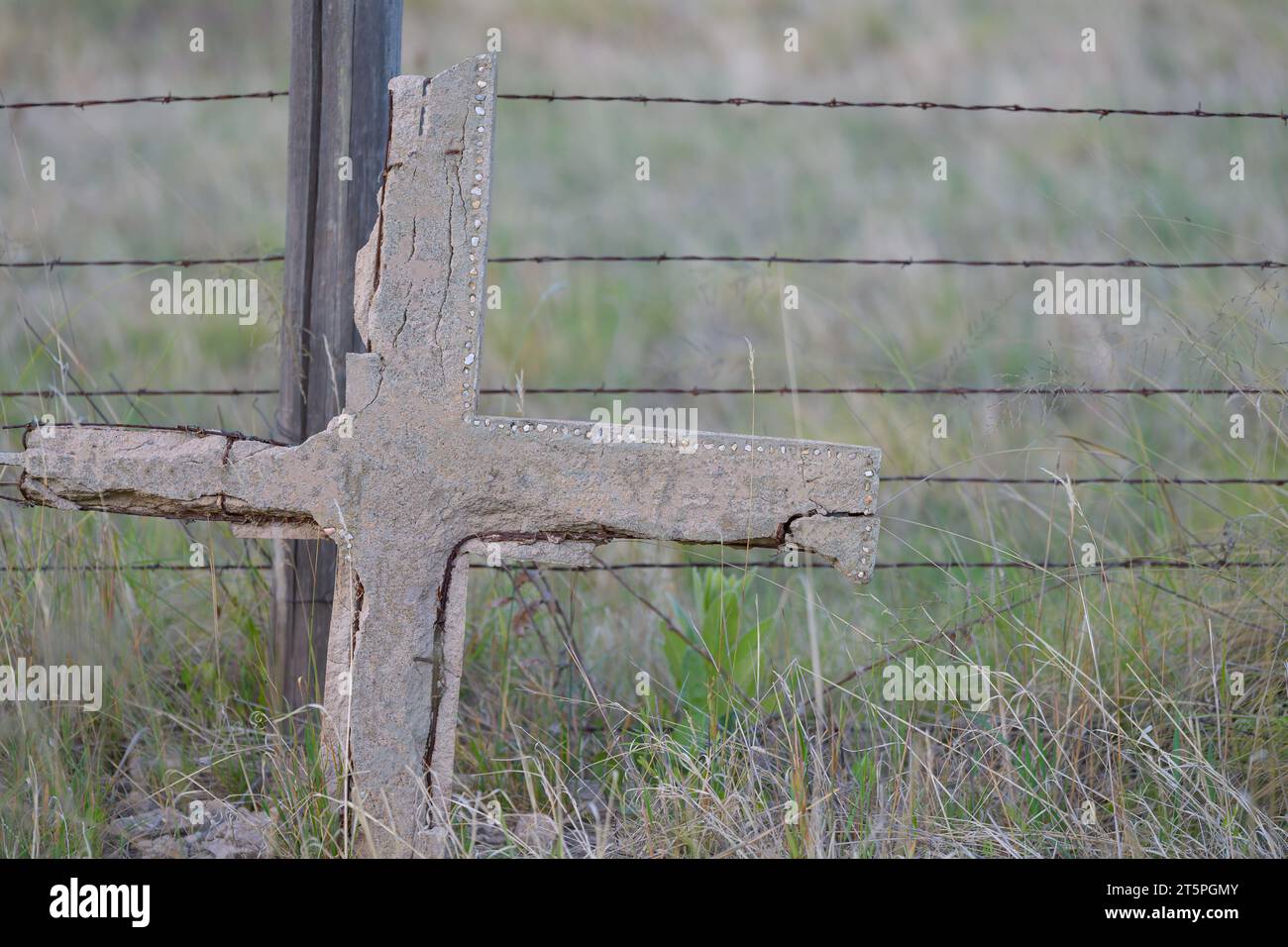 old concrete cross grave marker leaning on a barbed wire fence ...