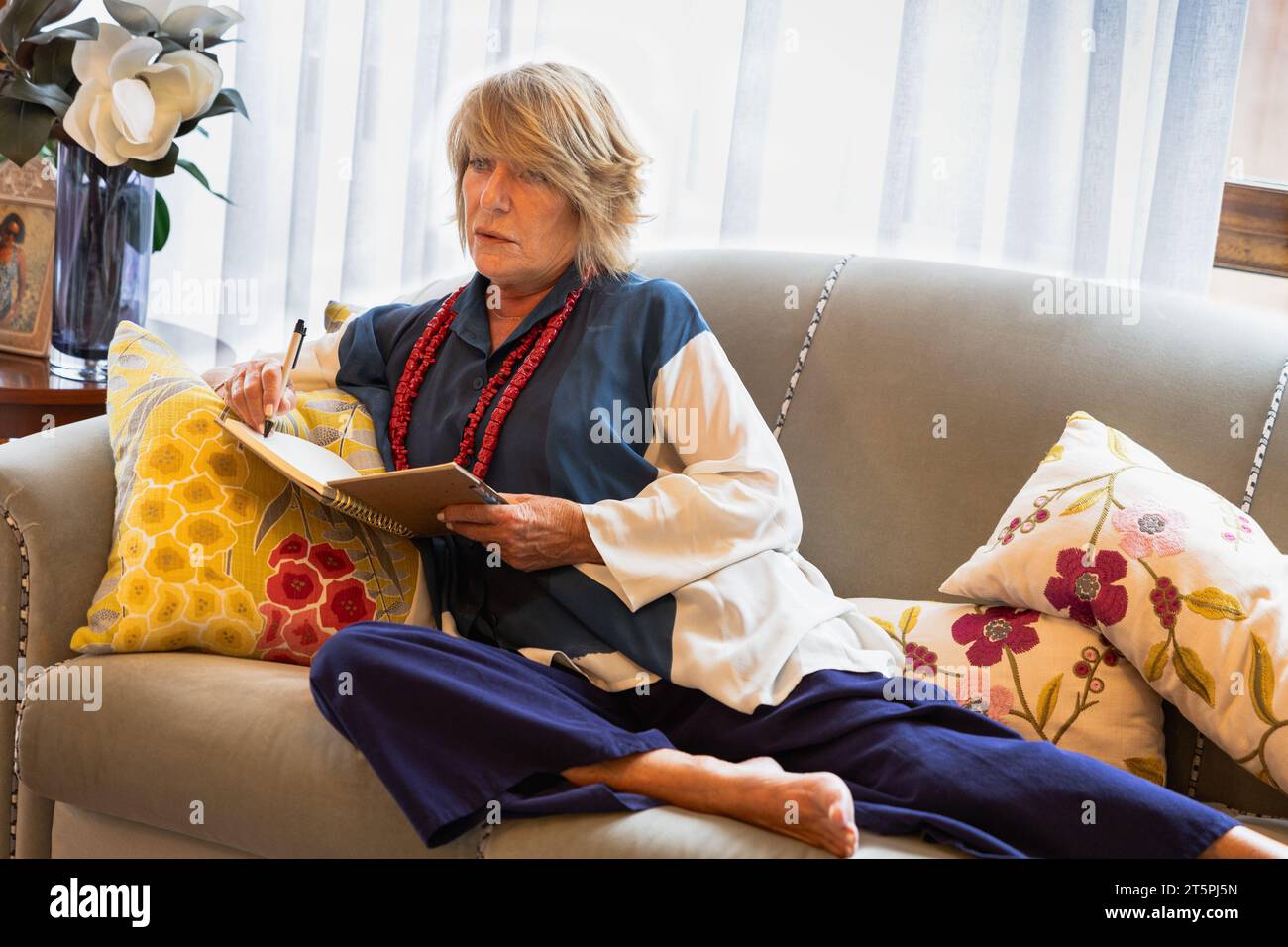 Relaxed mature woman sitting on sofa enjoying leisure time writing in ...