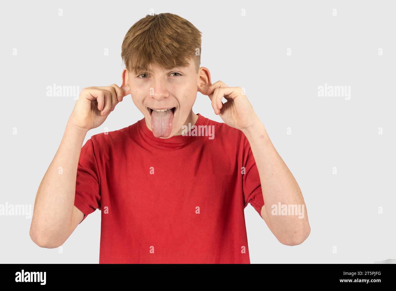 A studio portrait of a goofy fifteen year old teenage boy pulling a ...