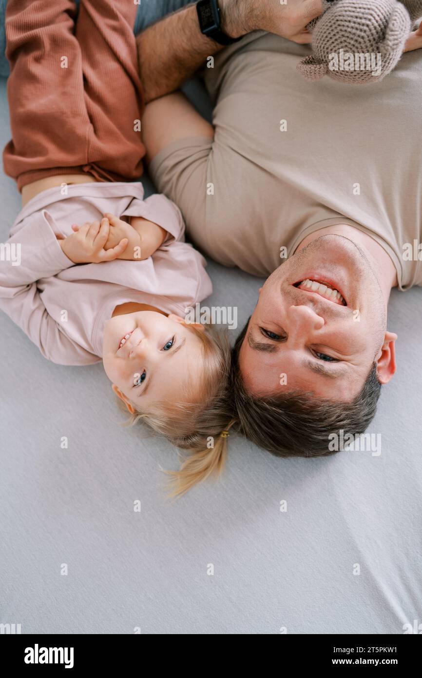 Laughing dad with a little girl lie upside down on the bed. Top view ...