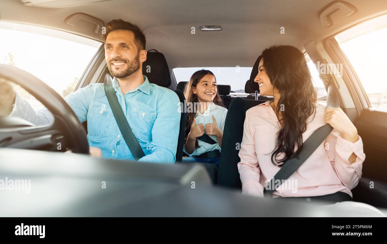 Happy family in car dad driving, daughter giving thumbs up, mom looking back at her child Stock ...