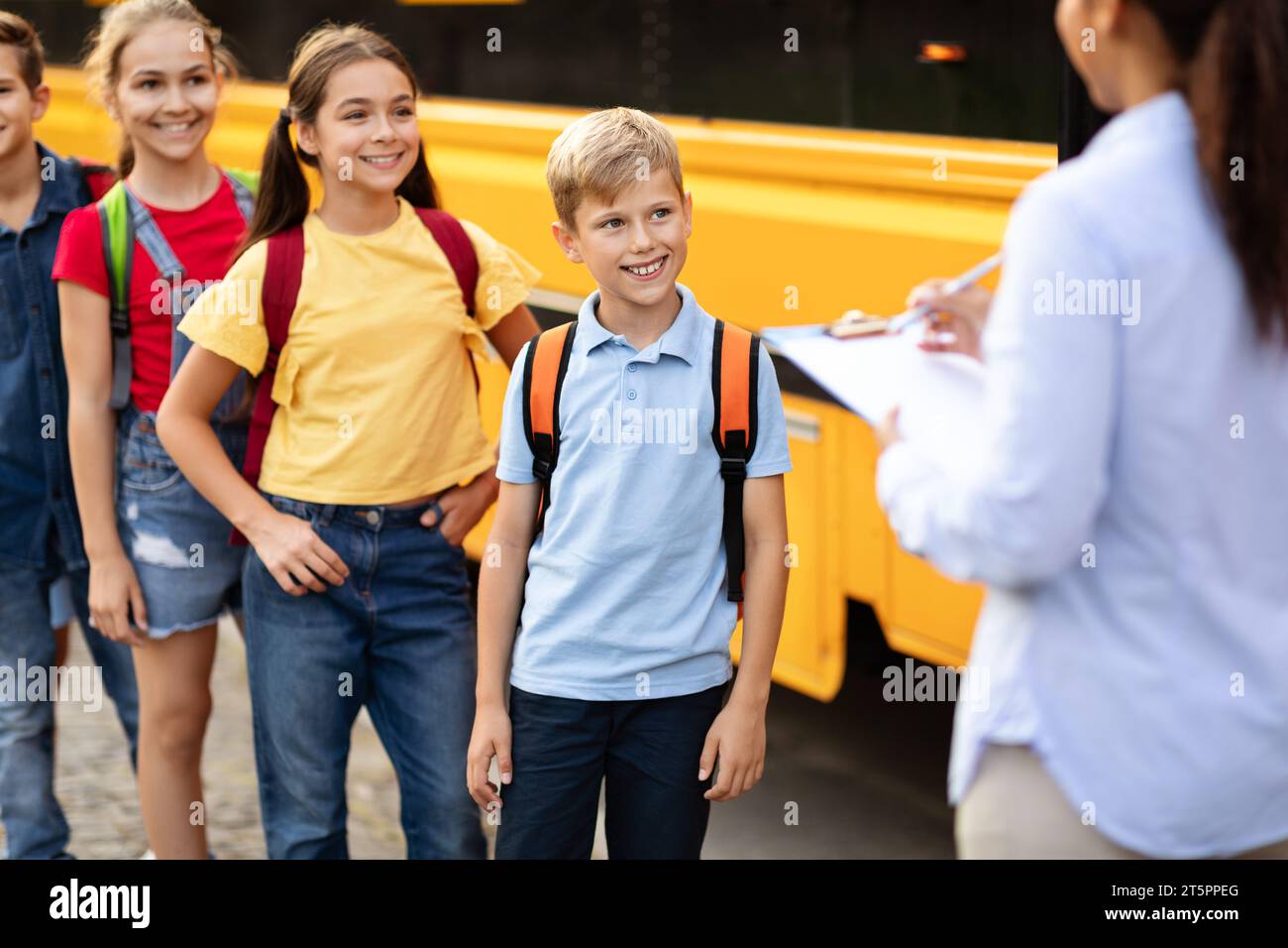 Black female teacher checking off names as children board the school ...
