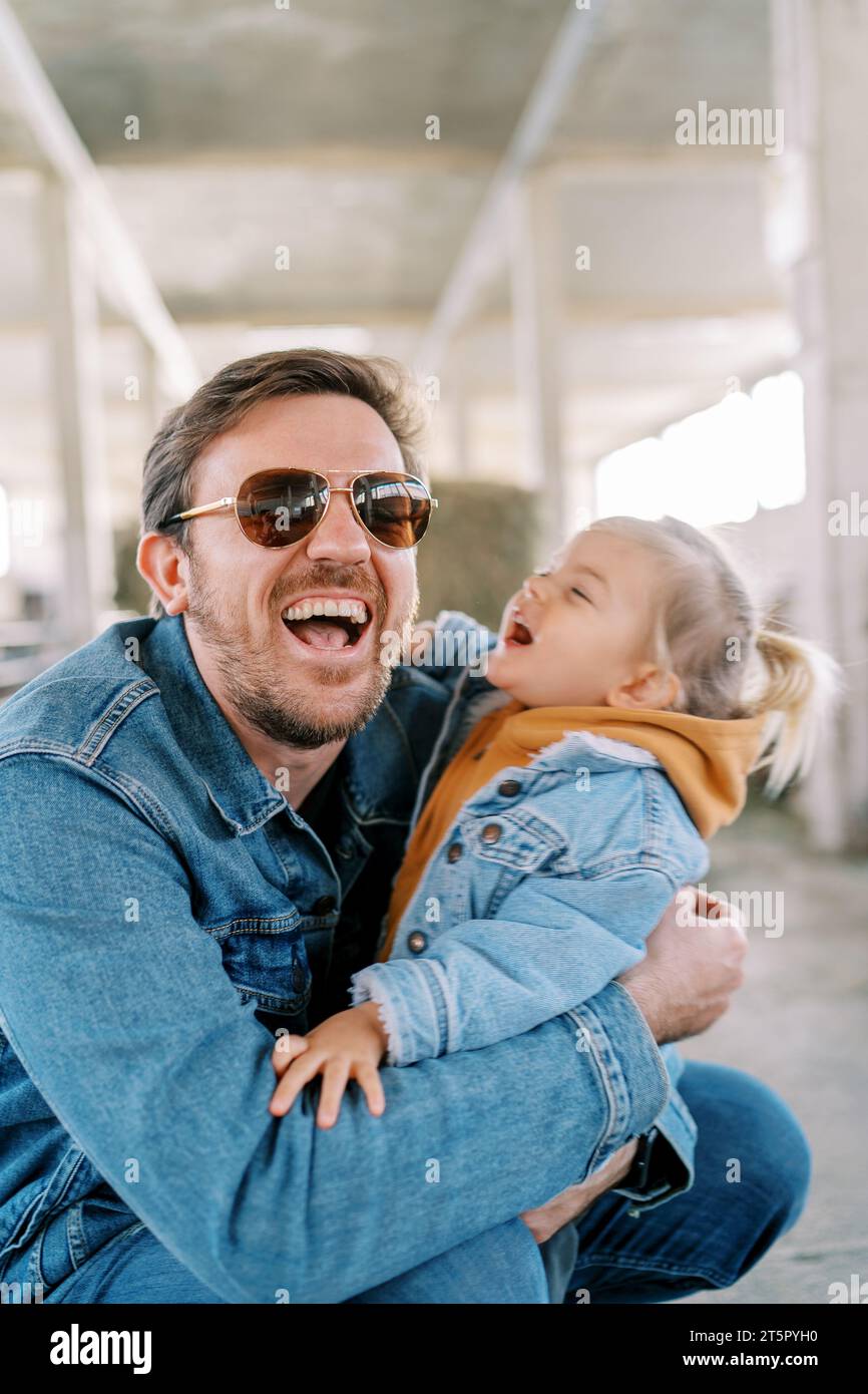 Laughing dad hugging a little girl laughing loudly while squatting on ...