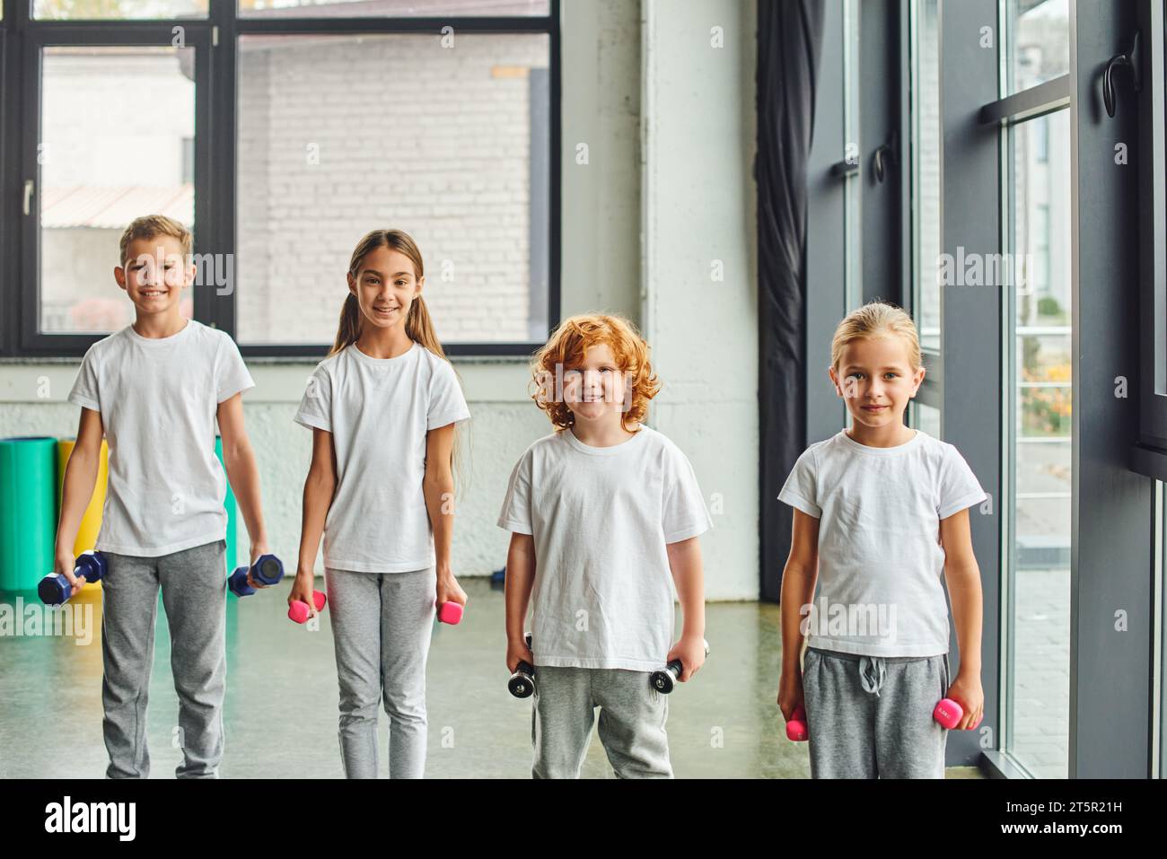 four cheerful little children posing with dumbbells and smiling ...