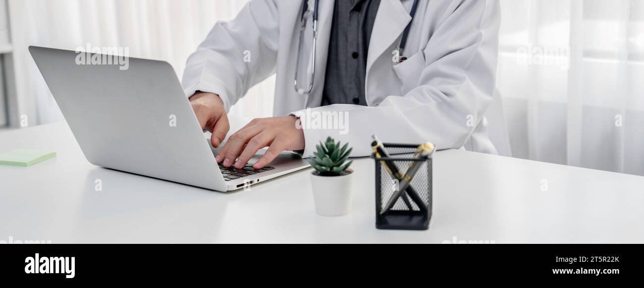 Doctor at hospital sit at his desk working on laptop diagnosing patient ...