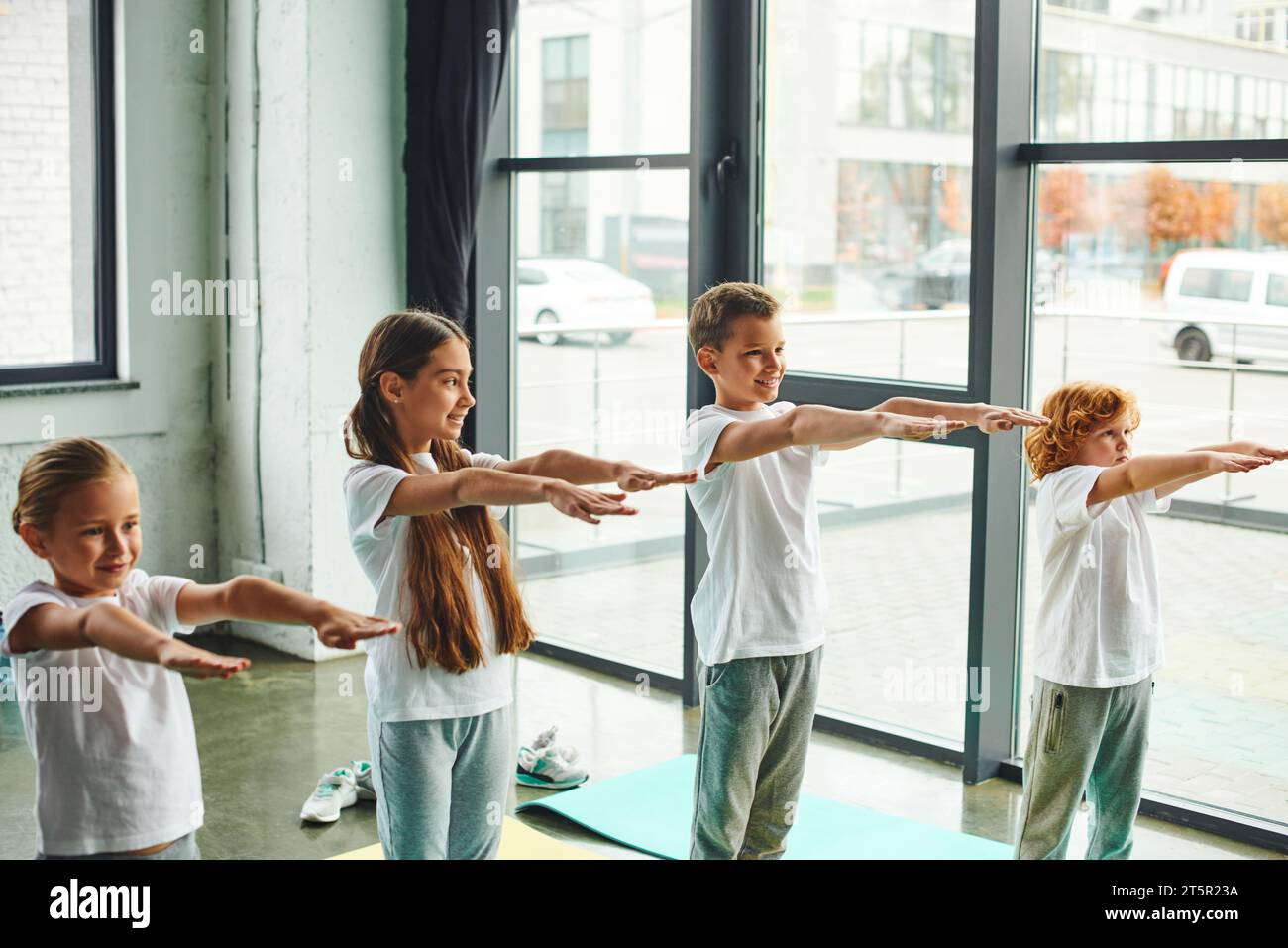 joyous little children in sportswear stretching their arms in gym with ...