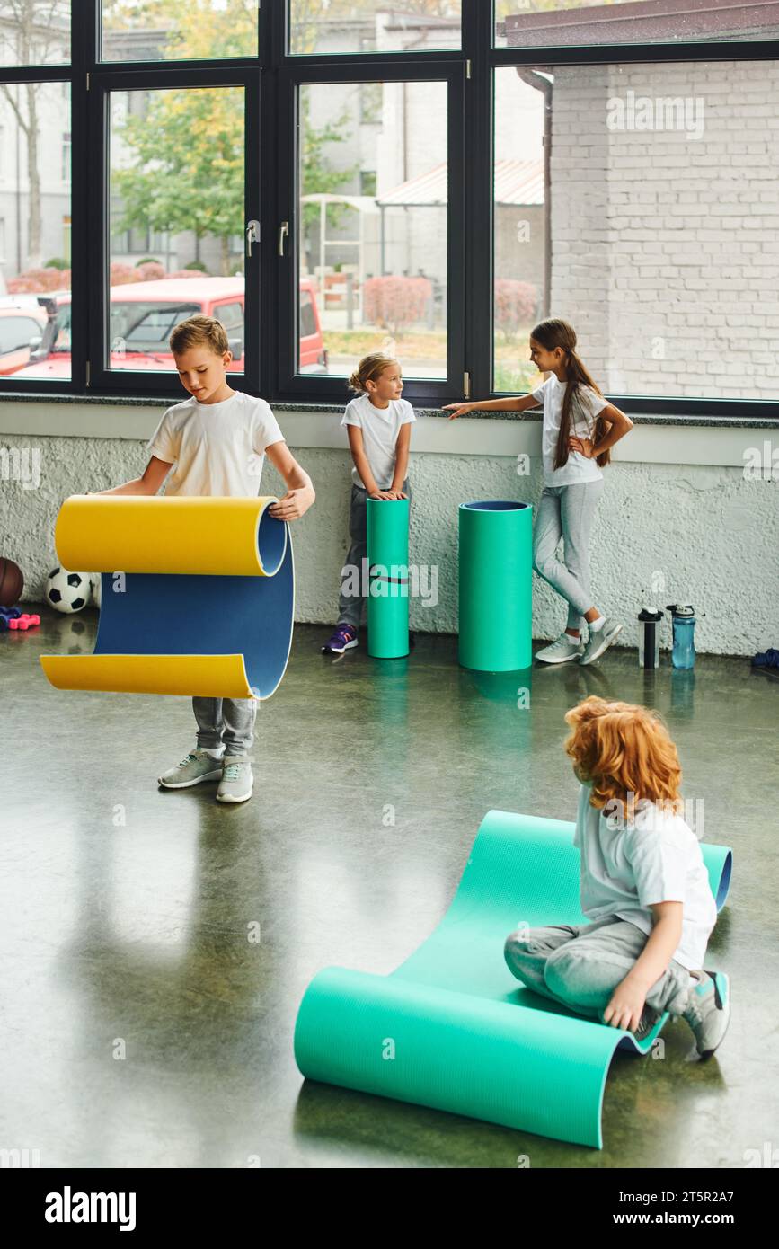 two little boys unfolding fitness mats while girls talking to each ...