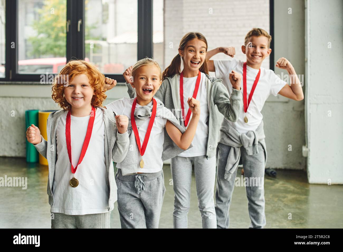 four joyful children in sportswear with medals cheering and smiling ...