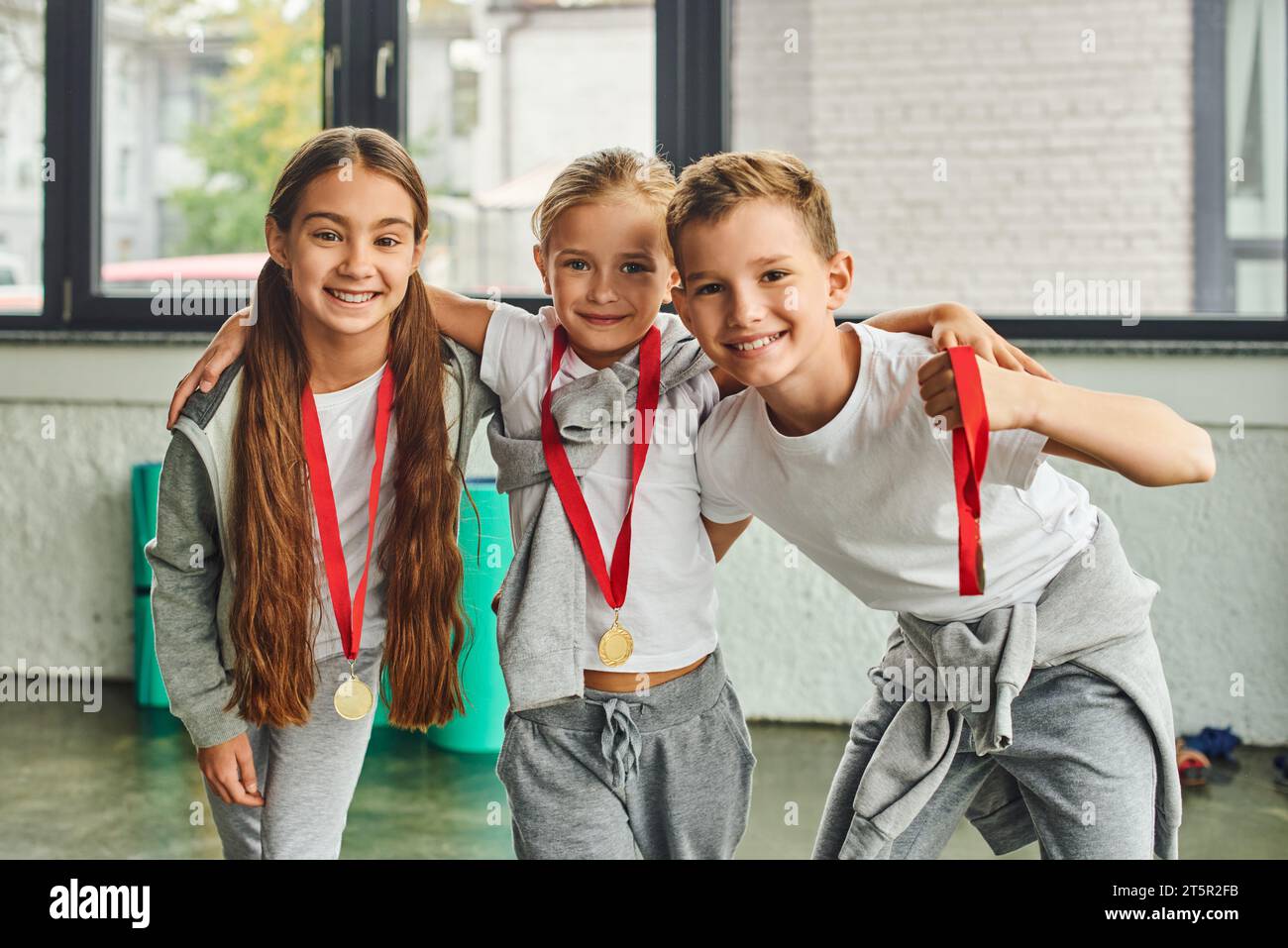 three little friends in sportswear with golden medals hugging and ...